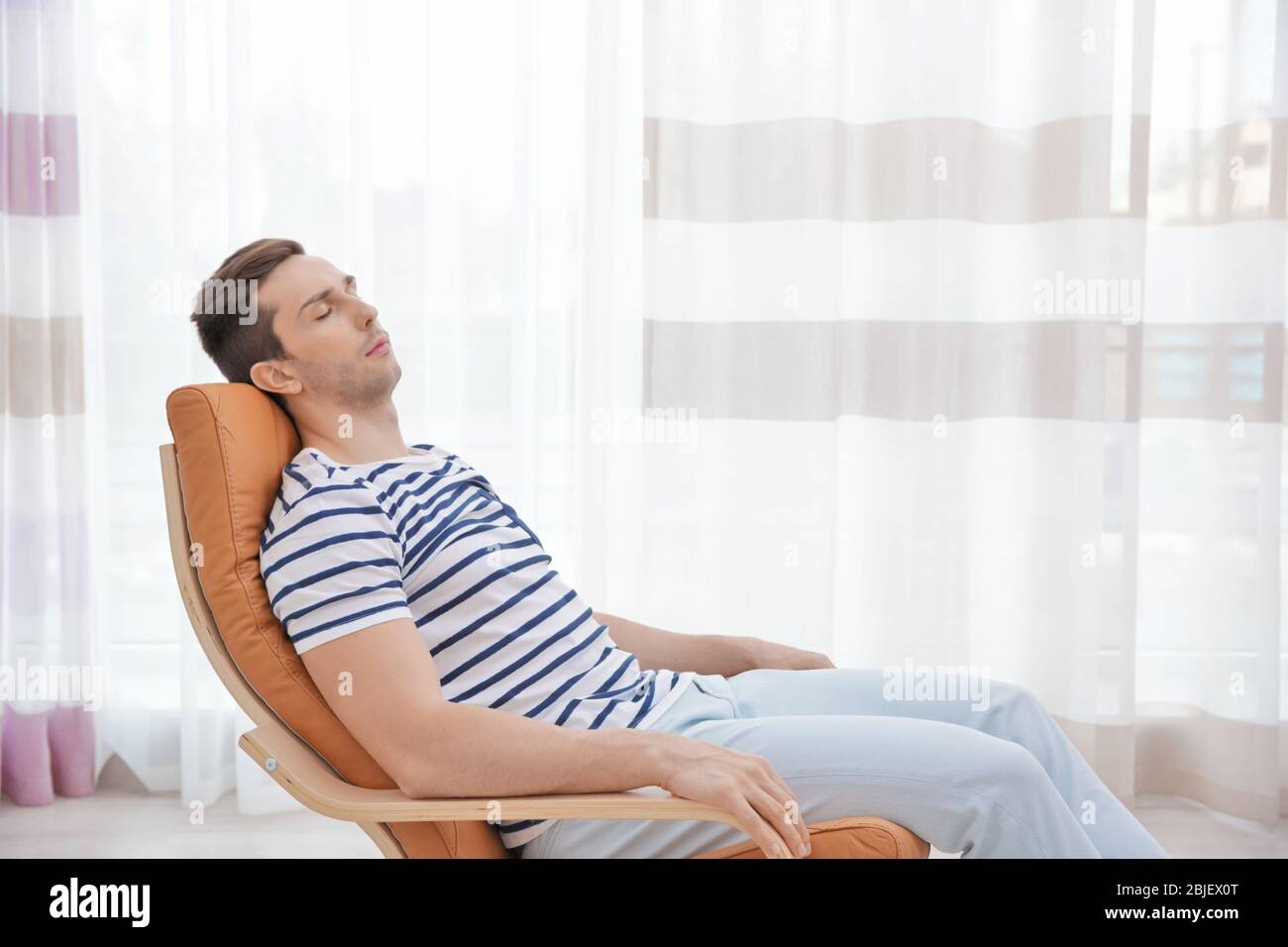 Young man resting on modern deck chair in light room Stock Photo - Alamy