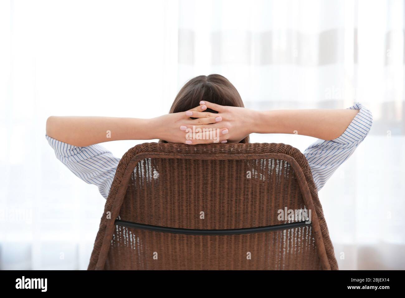 Rear view of relaxed woman with hands behind her head sitting on chair ...