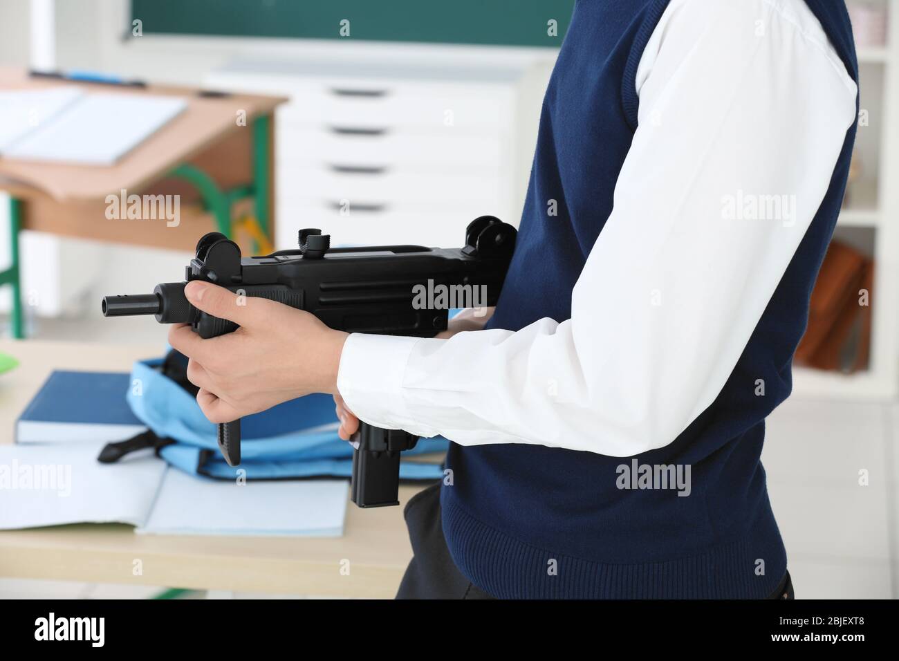 Closeup of schoolboy holding machine gun in classroom Stock Photo - Alamy