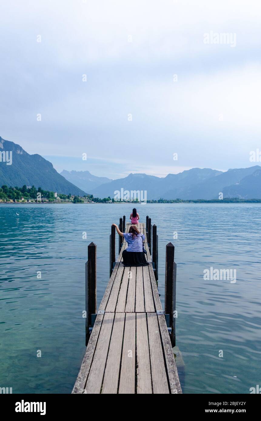A woman photographs her friend posing on a narrow wooden dock on the ...