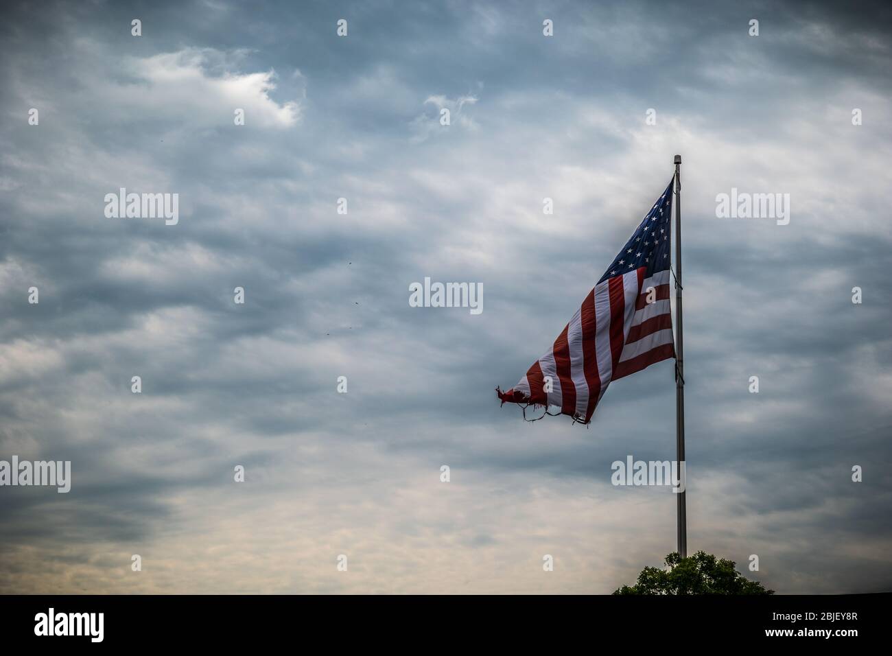 A large American flag ripped and torn flying proudly against the stormy ...