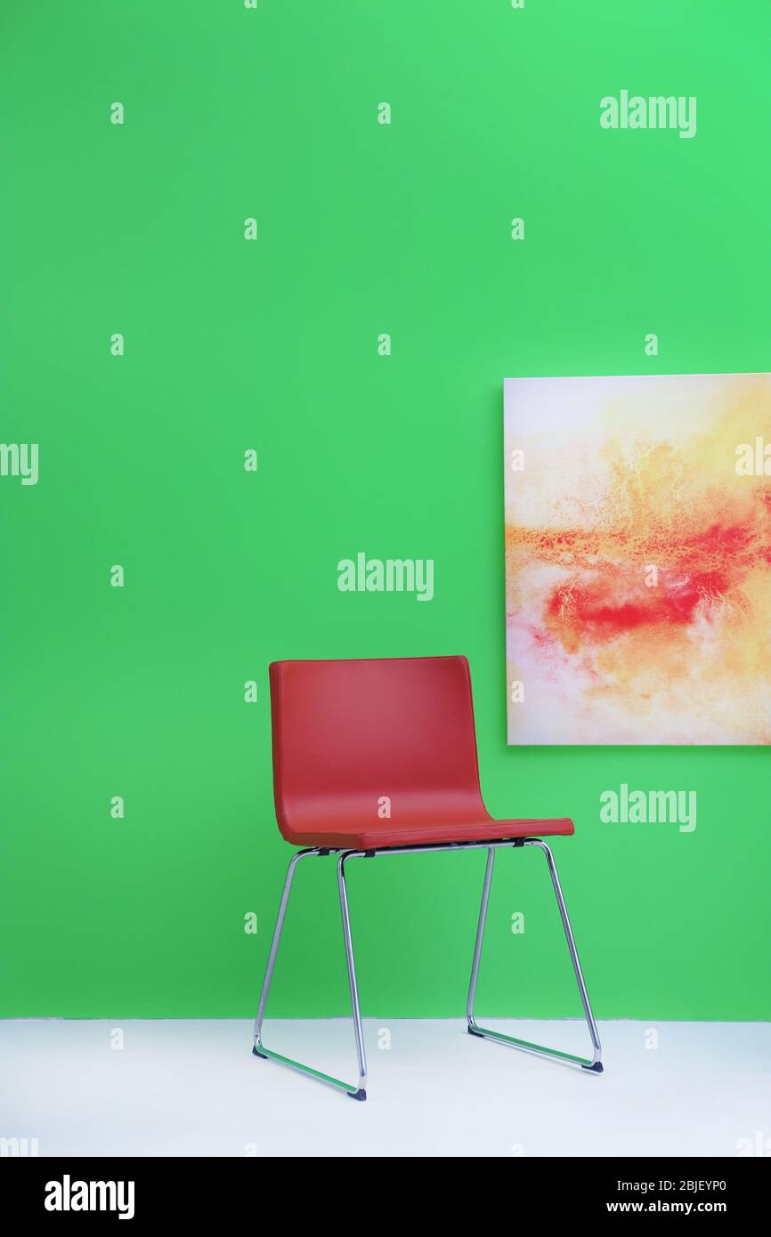 Modern red chair near green wall with abstract painting Stock Photo - Alamy