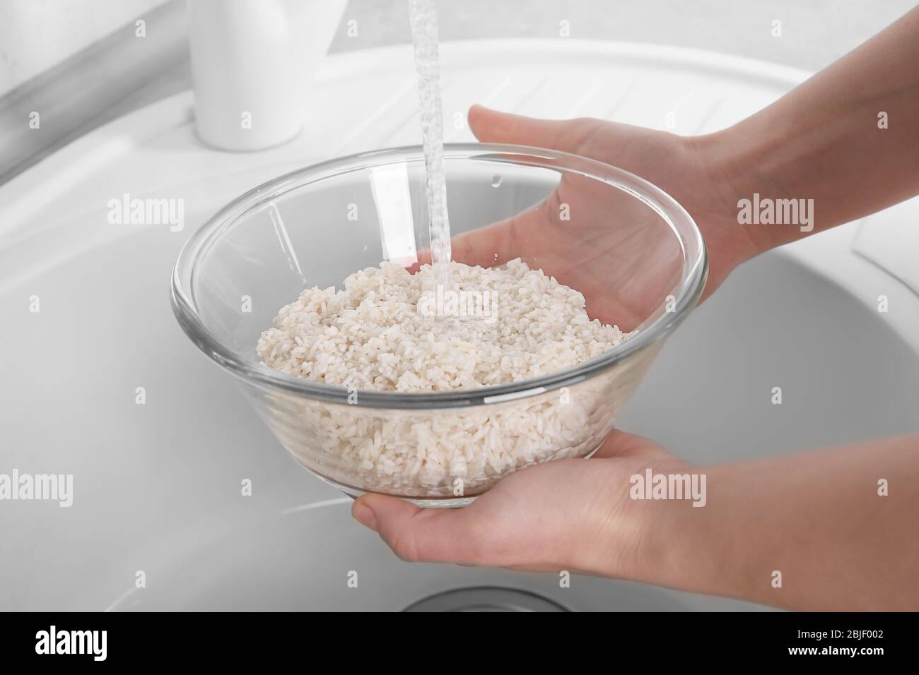 Woman rinsing rice in glass bowl under running water Stock Photo - Alamy