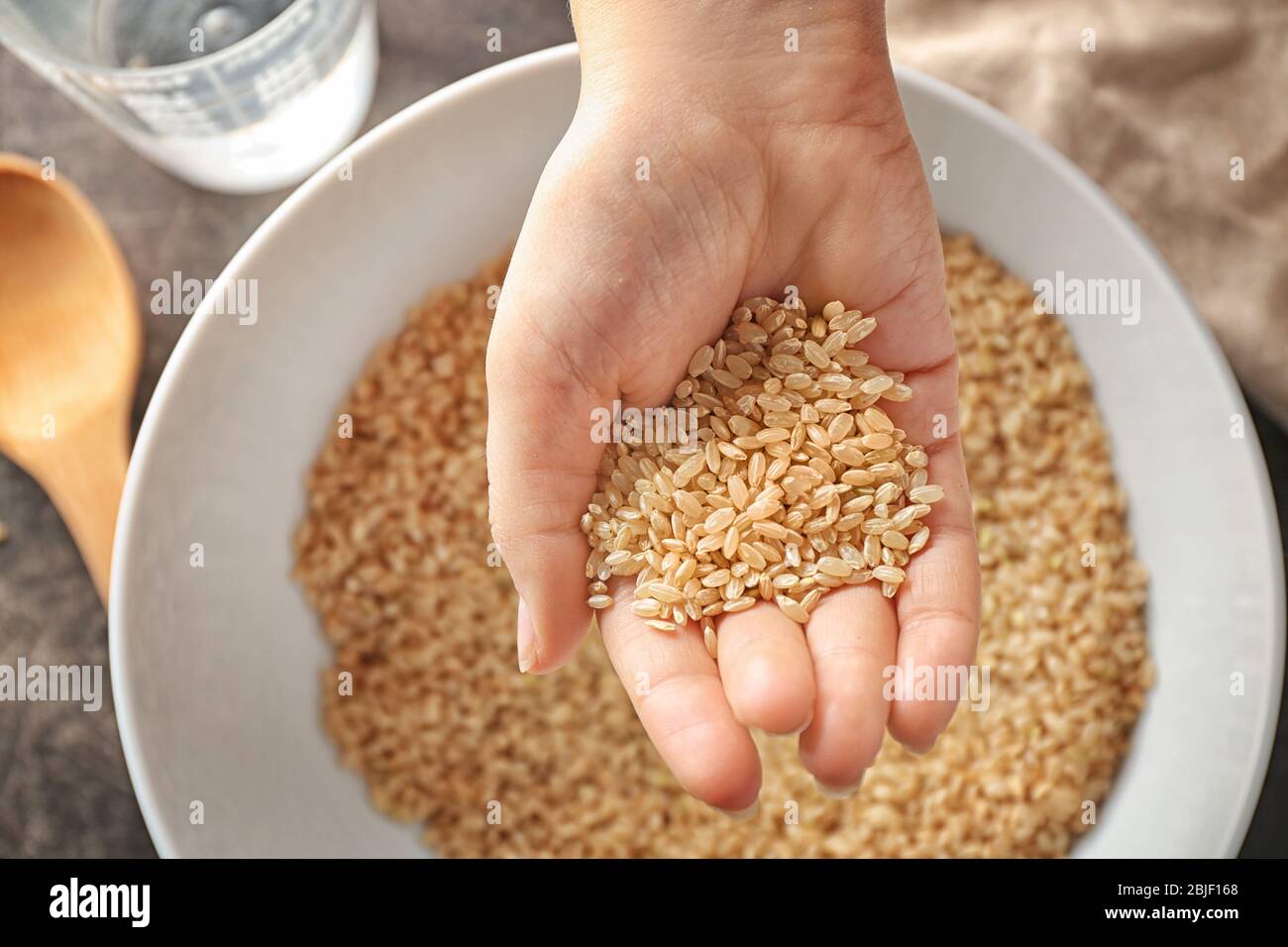 Woman holding heap of brown rice over white bowl Stock Photo - Alamy