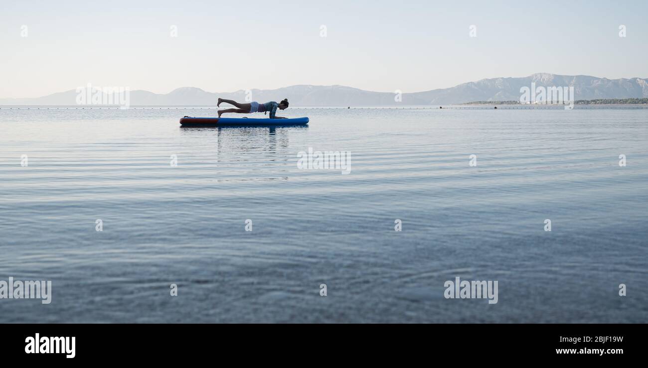 Fit young woman making plank position on sup board floating on calm ...