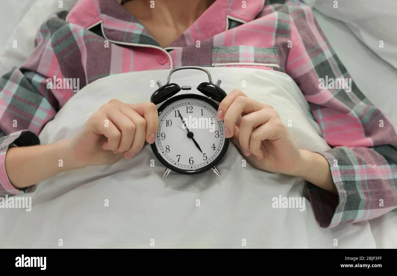 Young woman with alarm clock lying in bed at home. Sleep disorder ...