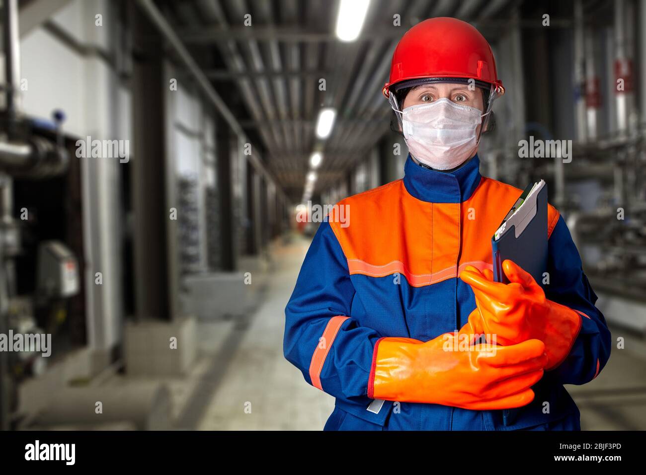 Female builder in a face mask and a construction helmet holds a folder ...