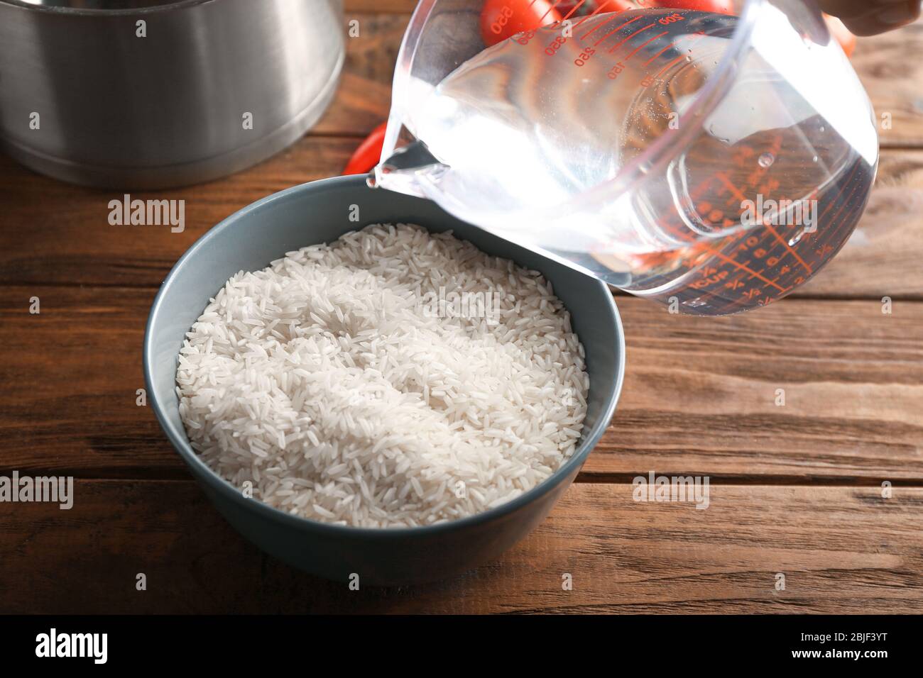 Pouring water into bowl with rice on kitchen table Stock Photo - Alamy