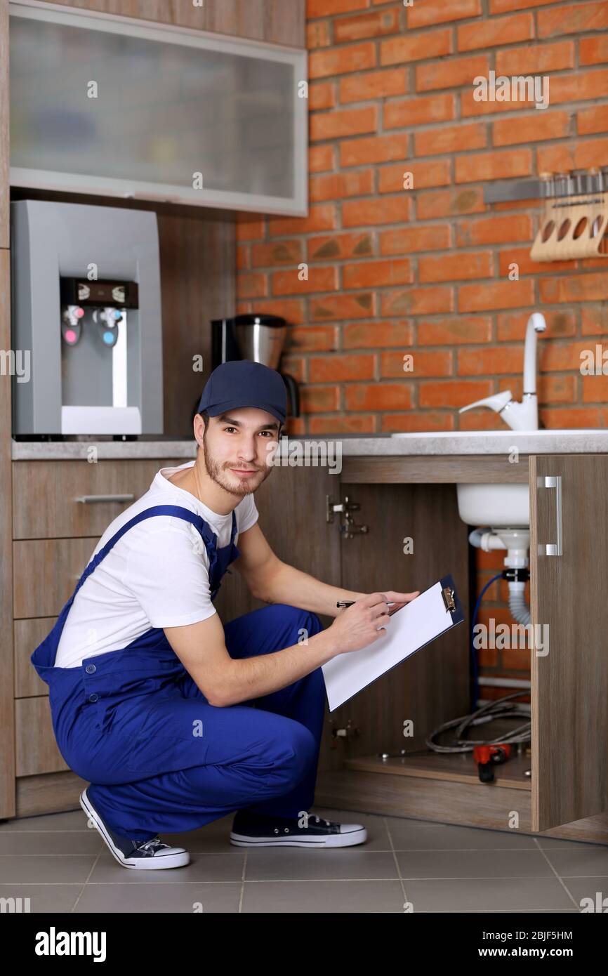 Handsome plumber with pen and clipboard in kitchen Stock Photo - Alamy