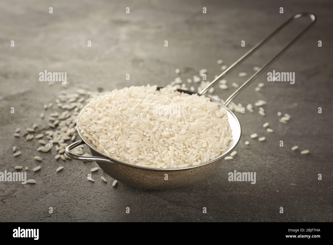 Metal sieve full of rice on grey table Stock Photo - Alamy