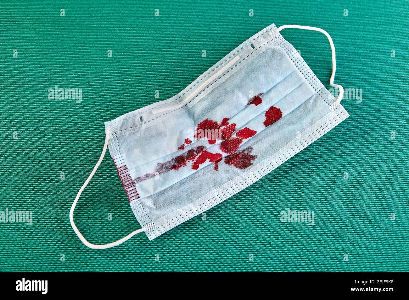 A used surgical mask or a disposable facemask with blood stains ...