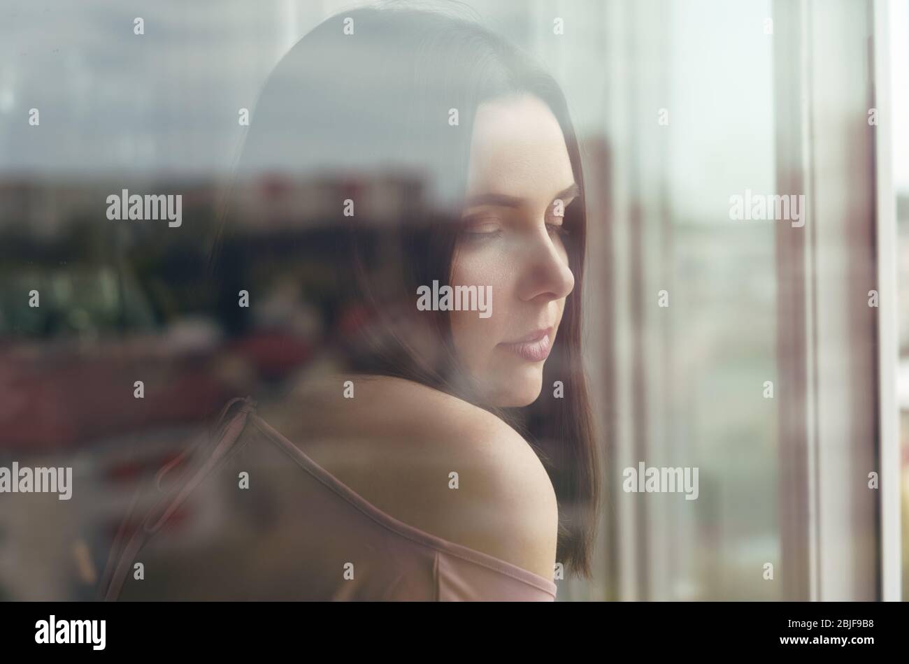Portrait of Brunette girl standing behind window with city reflection ...