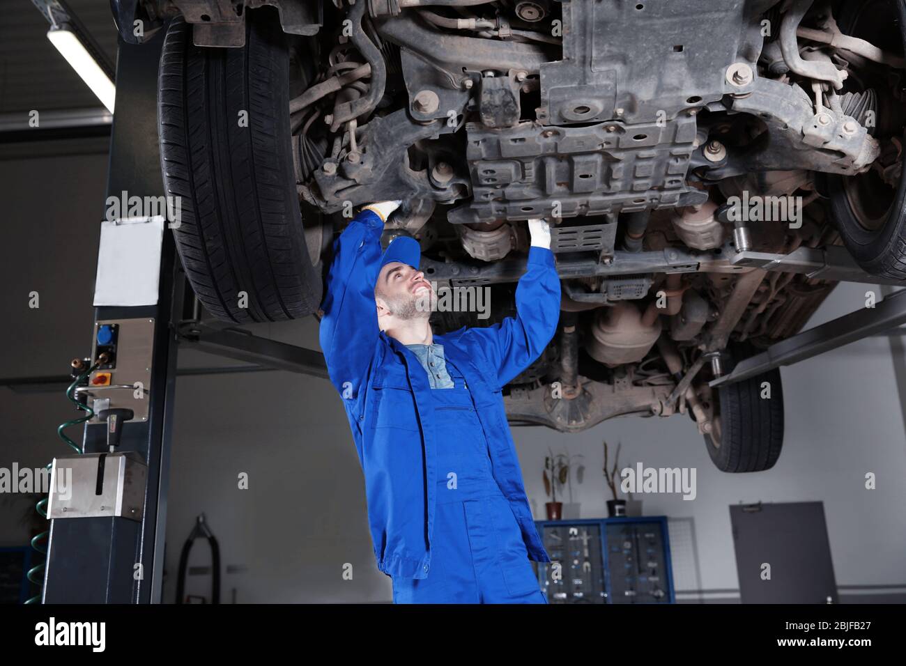 Young mechanic fixing wheel under car in service Stock Photo - Alamy
