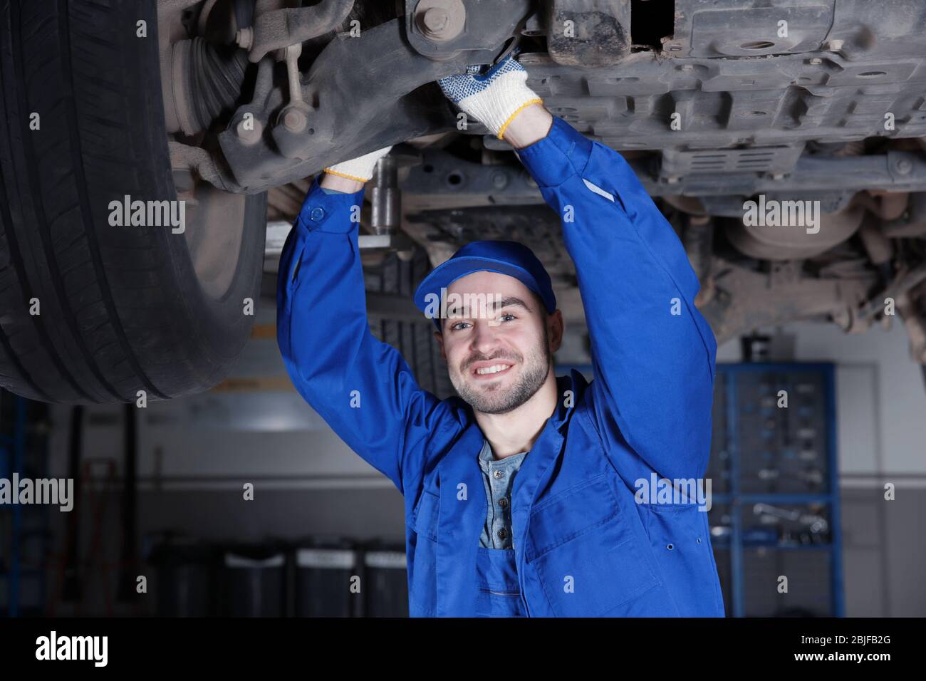 Young mechanic fixing wheel under car in service Stock Photo - Alamy