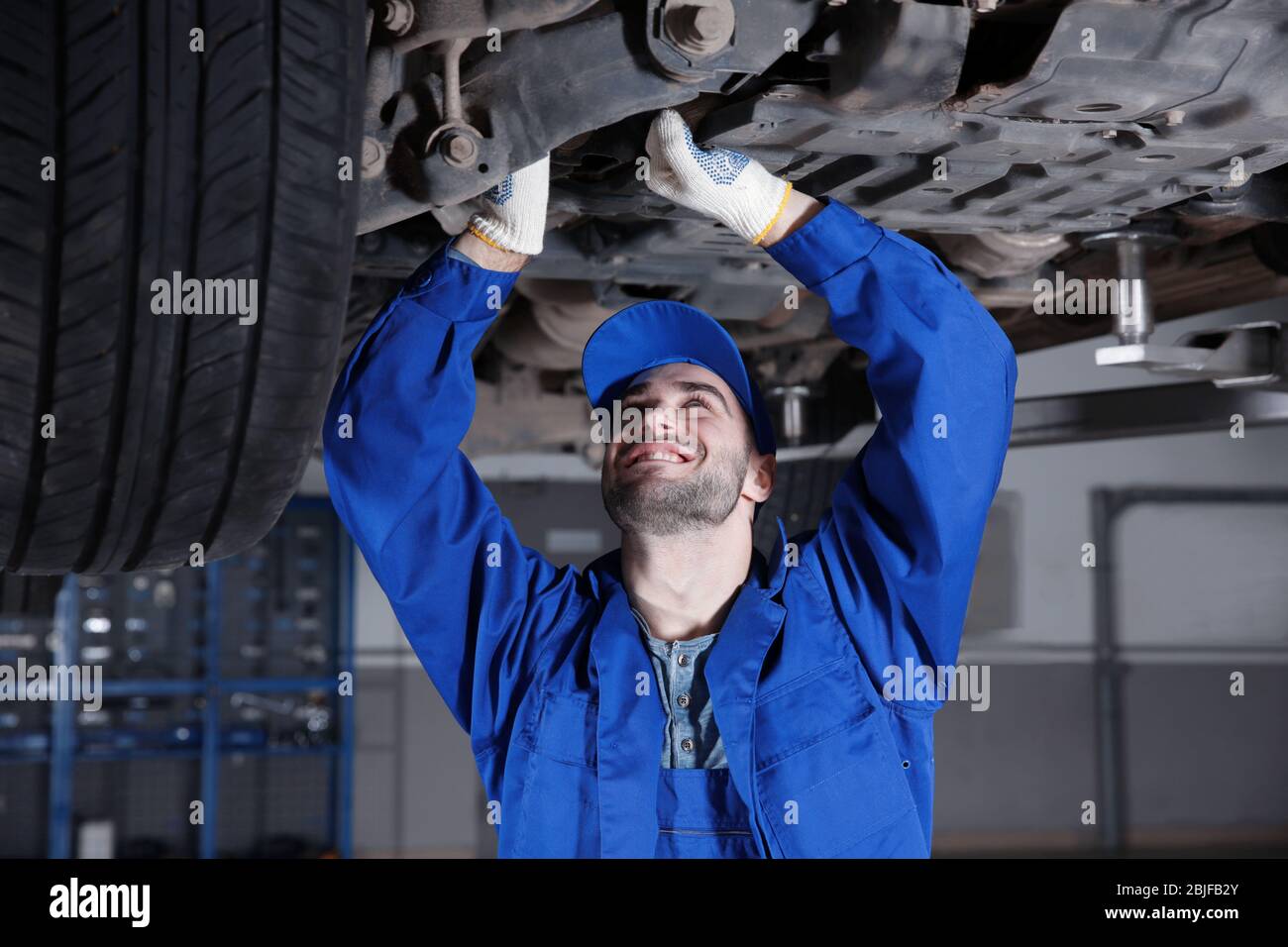 Young mechanic fixing wheel under car in service Stock Photo - Alamy