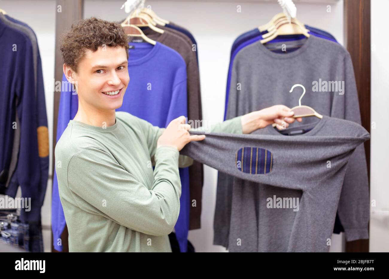 Handsome young man choosing clothes in modern shop Stock Photo - Alamy