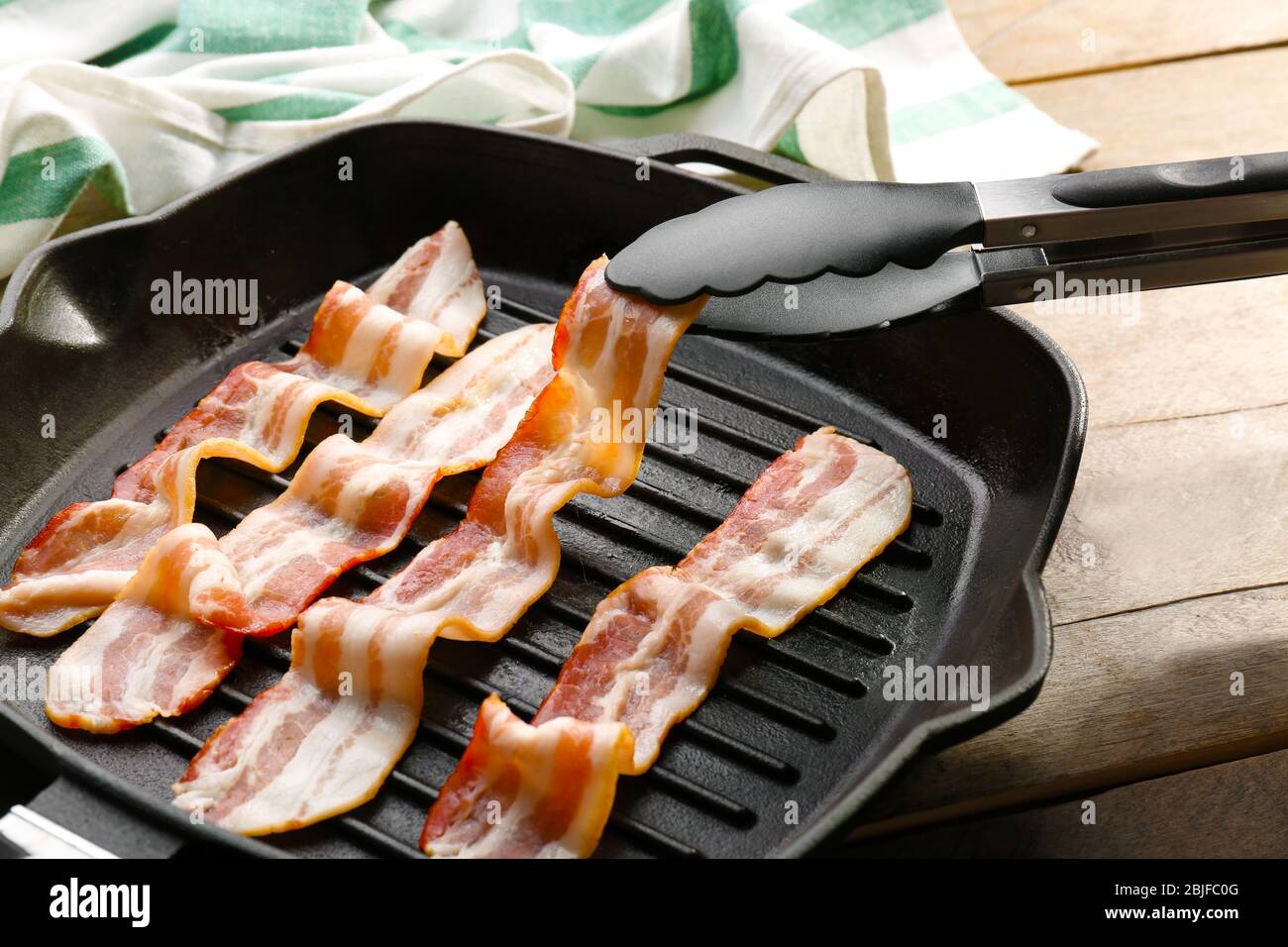 Placing bacon slice in pan with tongs, closeup Stock Photo - Alamy