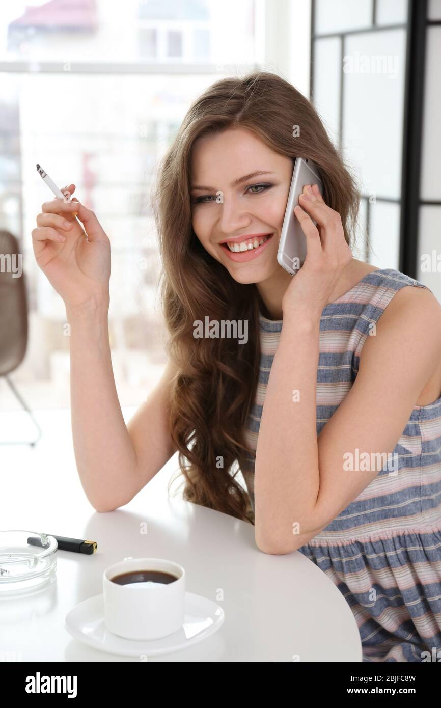 Young woman smoking and speaking on telephone in light room Stock Photo ...
