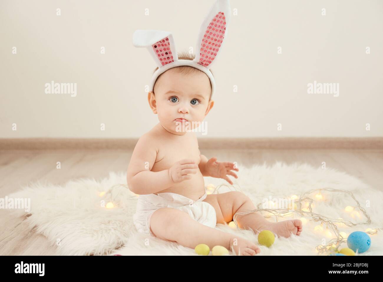Cute little baby wearing bunny ears sitting on furry rug with garland ...