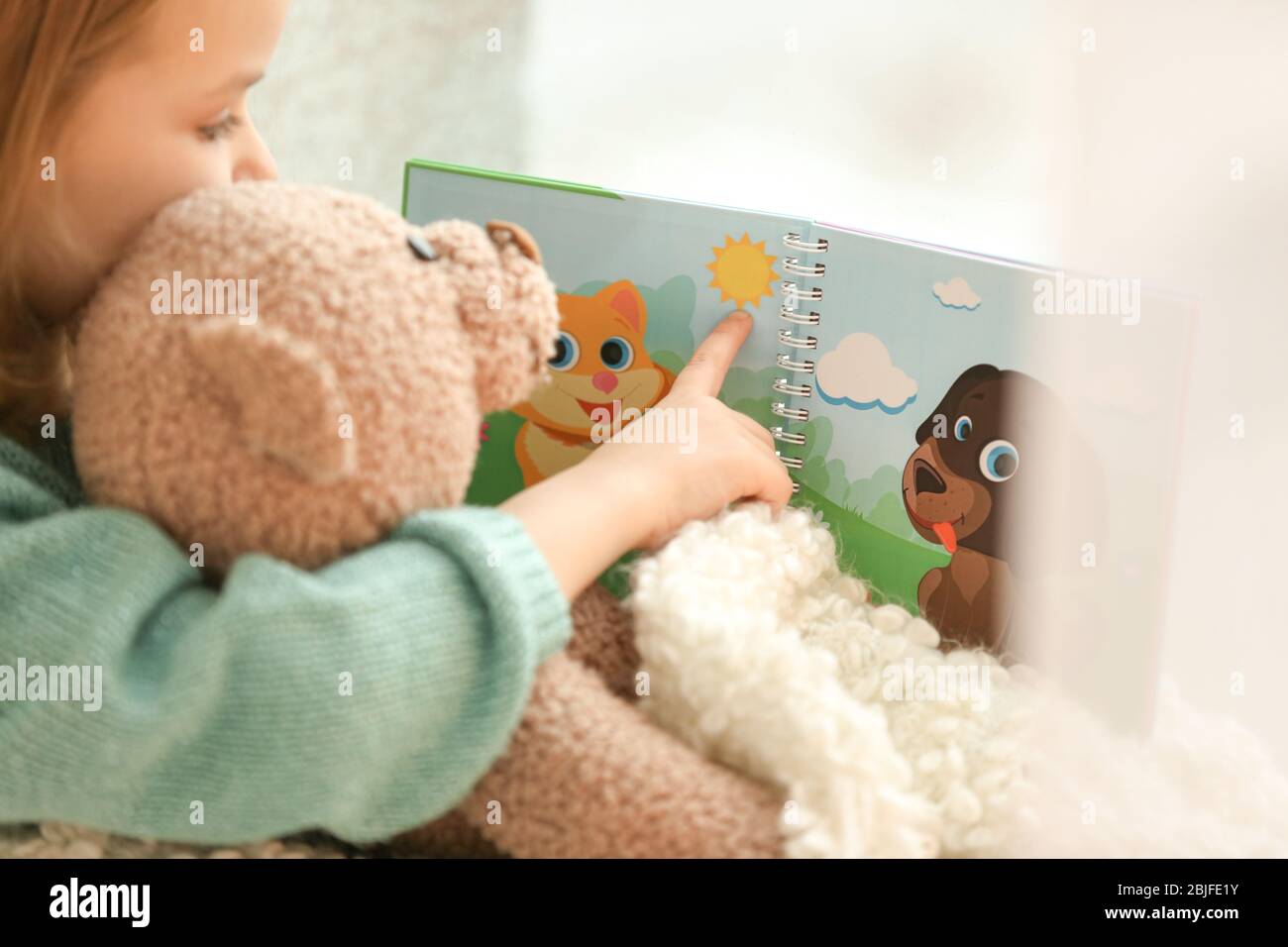 Cute little girl with teddy bear and book near window at home Stock ...