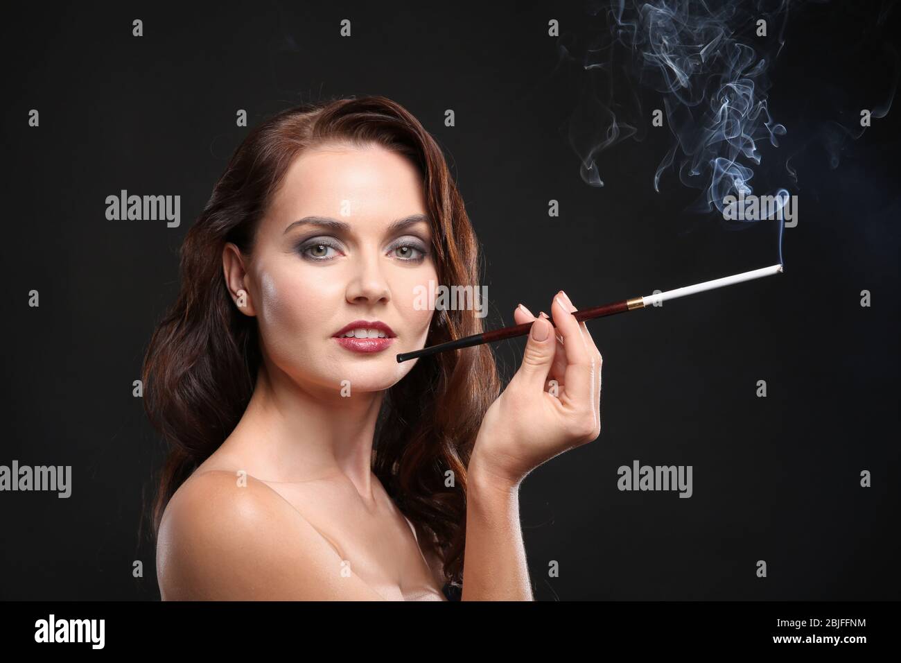Beautiful woman smoking cigar on dark background Stock Photo - Alamy