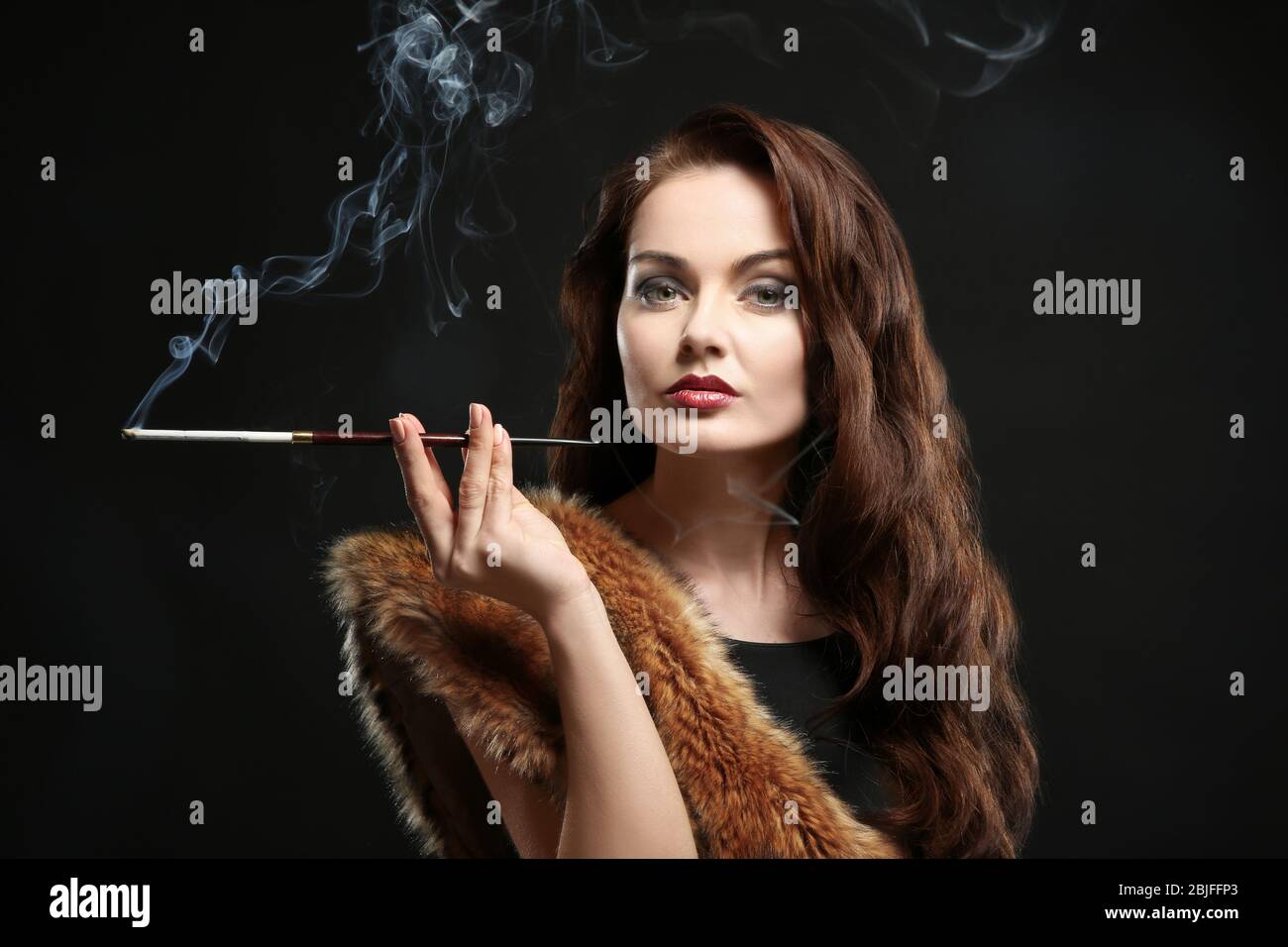 Beautiful woman smoking cigar on dark background Stock Photo - Alamy