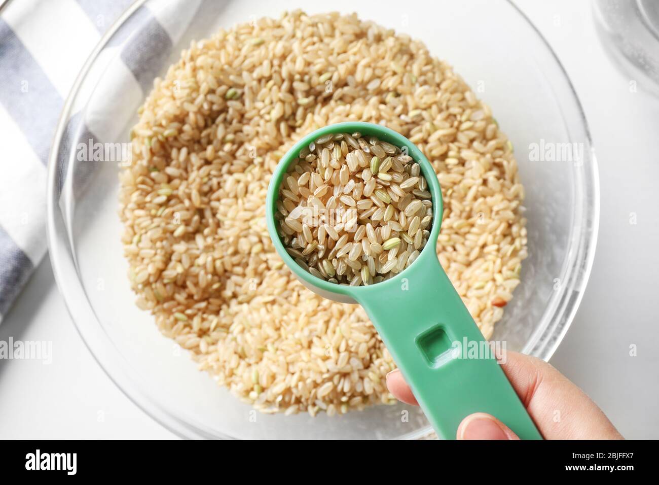 Measure scoop full of brown rice taken from glass bowl Stock Photo - Alamy