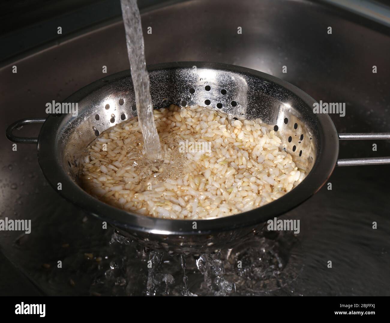 Washing brown rice with water in colander Stock Photo - Alamy