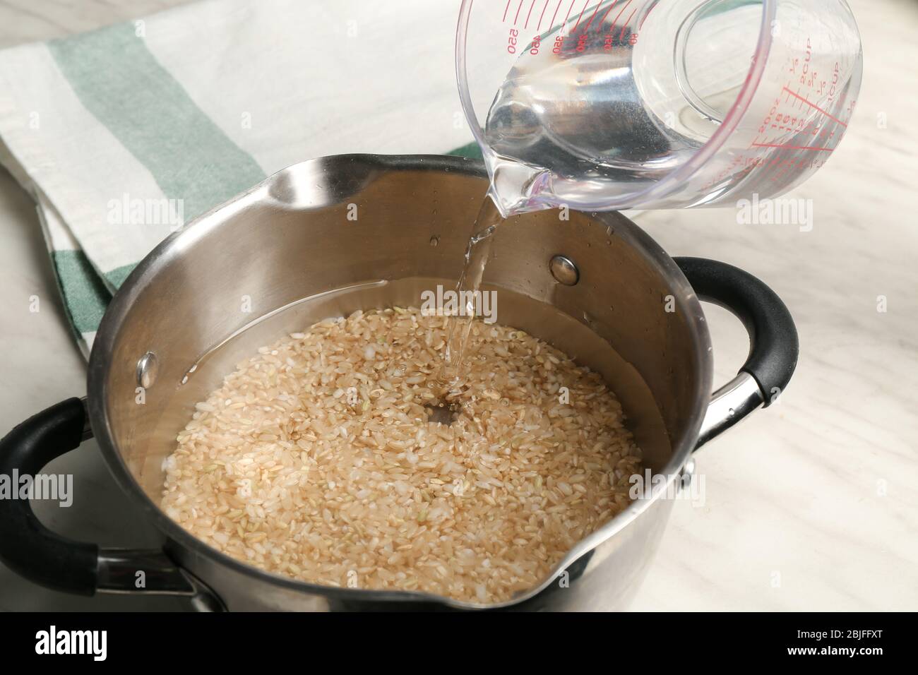 Pouring water into saucepan with brown rice on kitchen table Stock ...