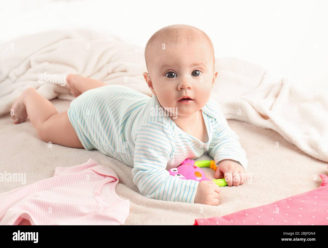 Adorable baby with toy rattle lying on bed Stock Photo - Alamy