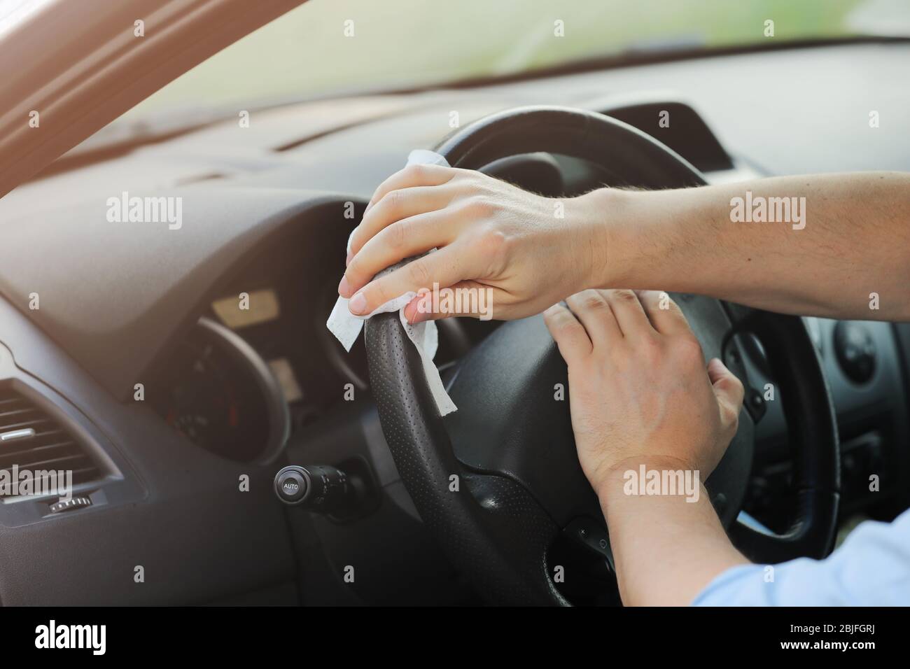 Driver using wet wipe for disinfecting car steering wheel against virus ...