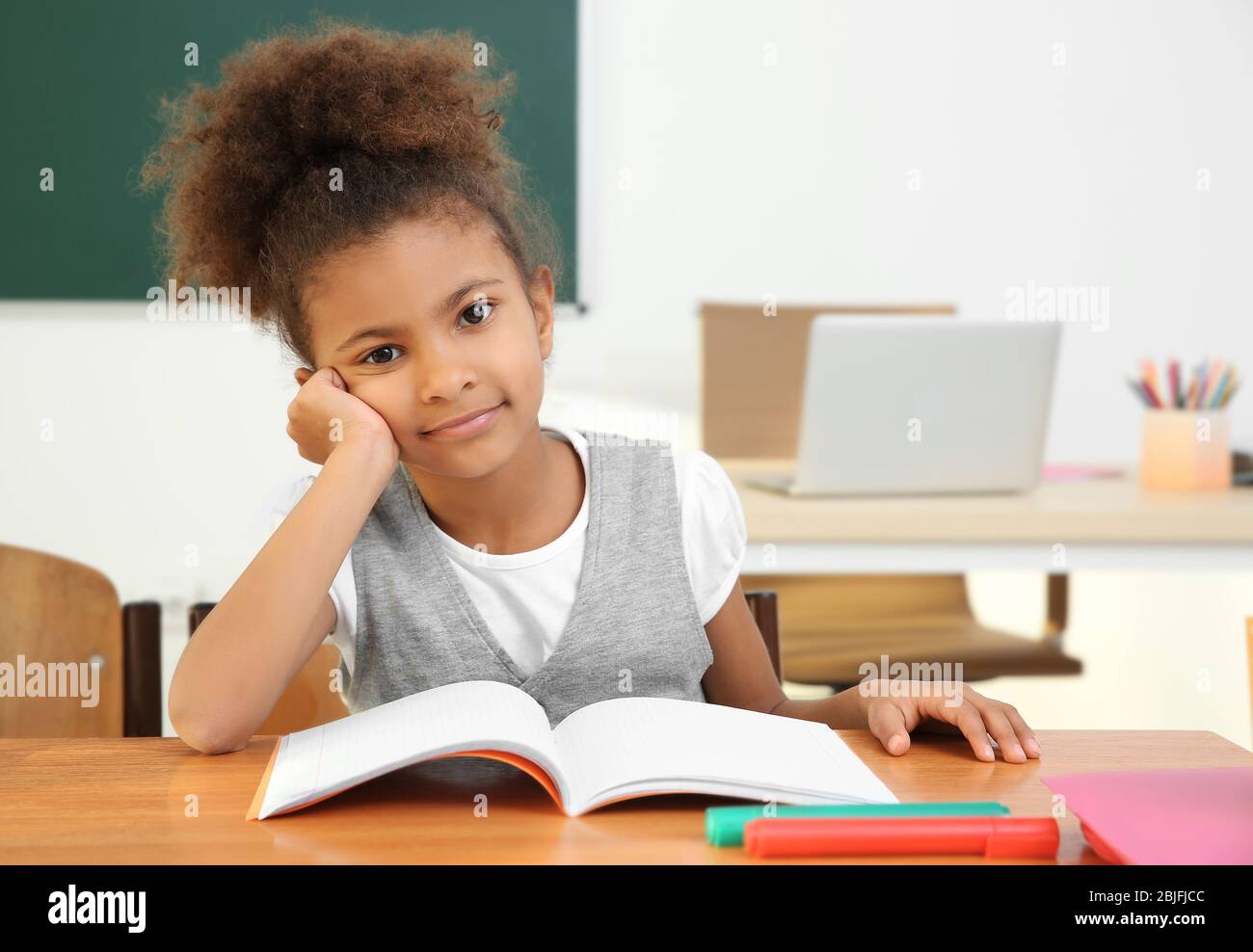 Portrait of beautiful African elementary schoolgirl sitting in ...