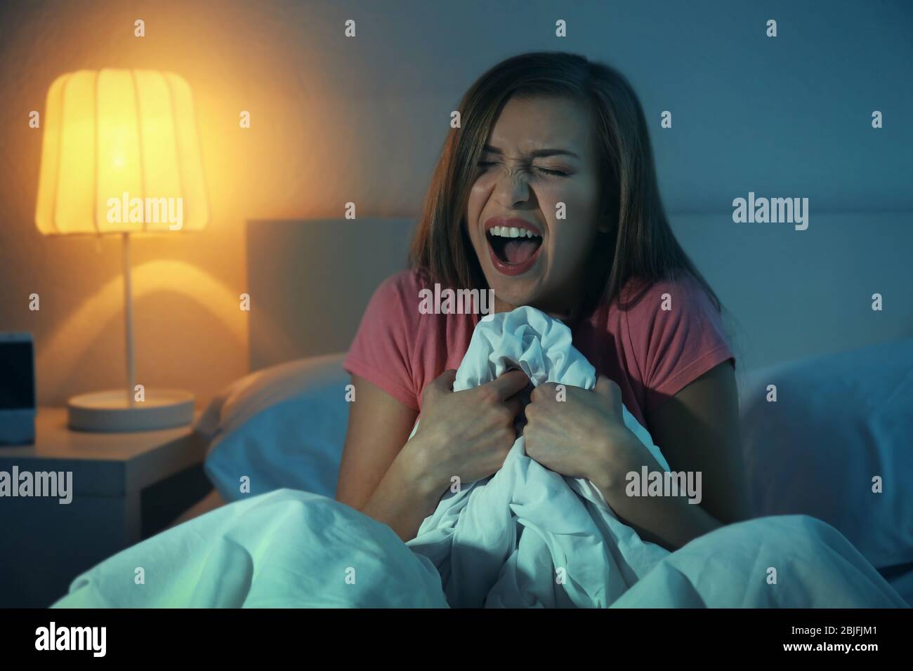 Young scared woman sitting on bed at home Stock Photo - Alamy