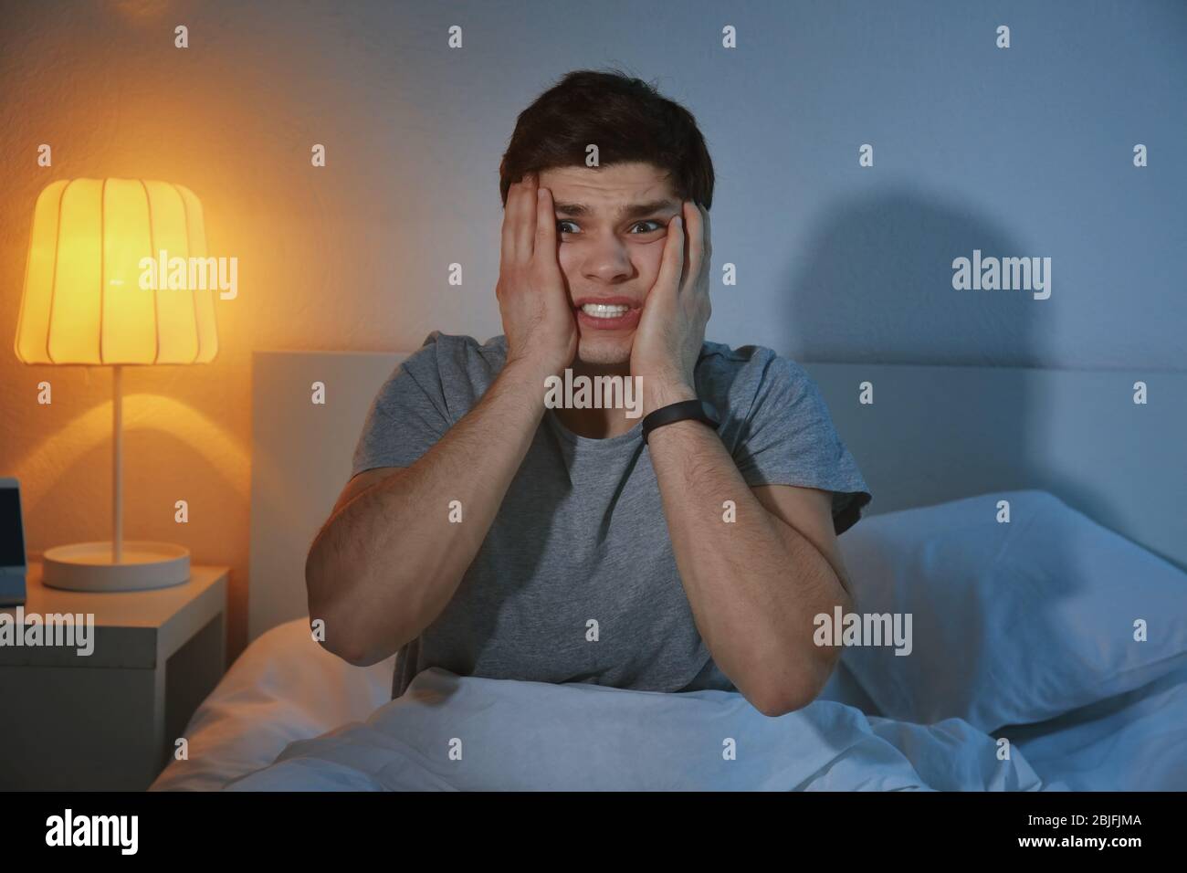 Young scared man sitting on bed at home Stock Photo - Alamy