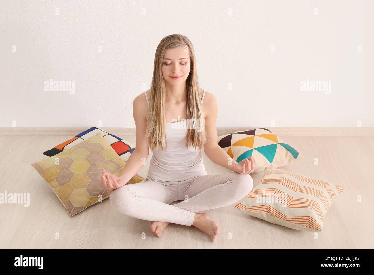 Beautiful young woman meditating prior to sleep while sitting on floor ...