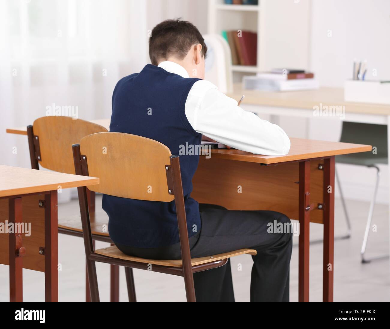 Incorrect posture concept. Schoolboy sitting at desk in classroom Stock ...
