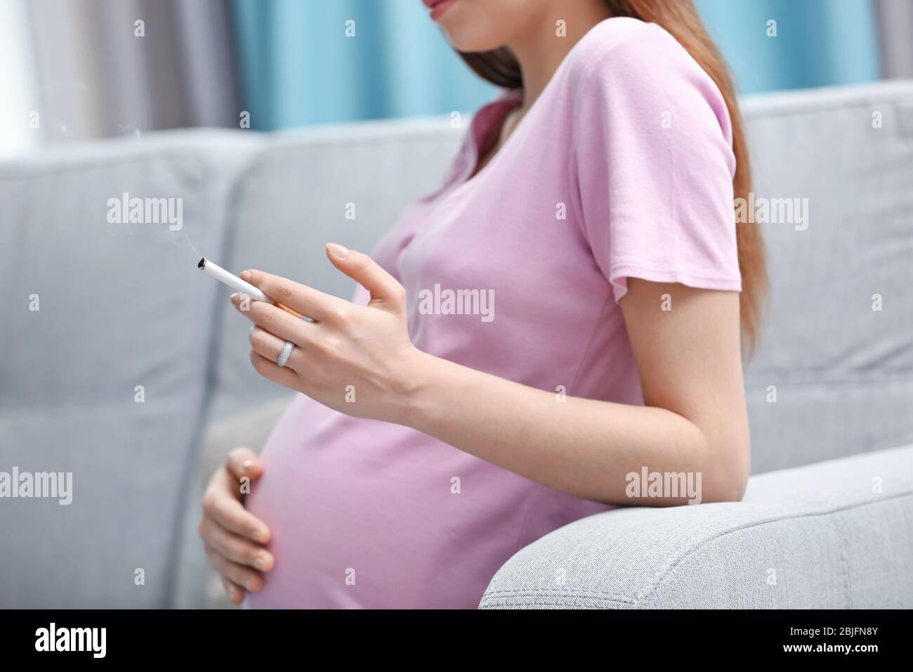 Pregnant woman smoking cigarette sitting on sofa at home Stock Photo ...