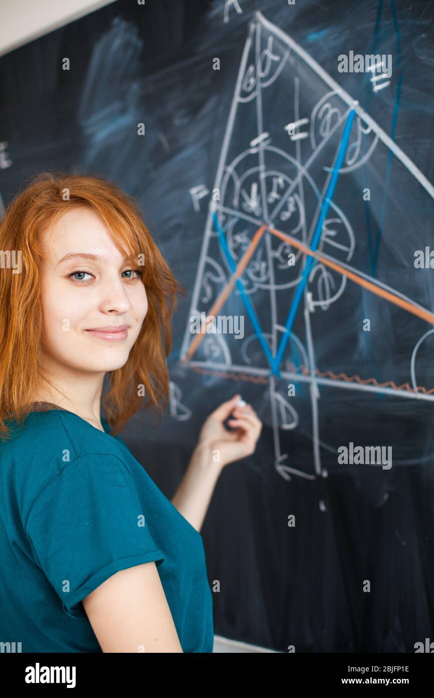 Portrait of a pretty young college student writing on the blackboard ...