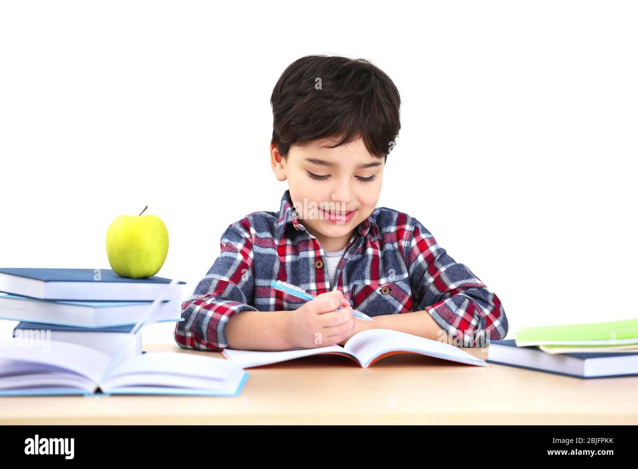Cute little boy writing in notebook while sitting at table Stock Photo ...