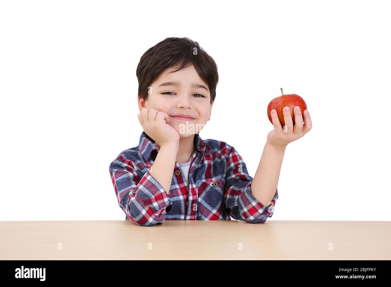 Cute little boy with apple sitting at table, on white background Stock ...
