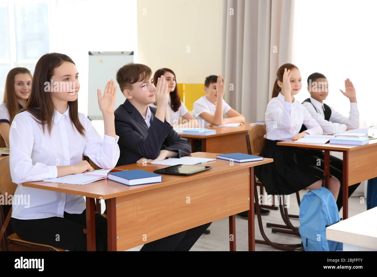 Pupils raising hands to answer in classroom Stock Photo - Alamy