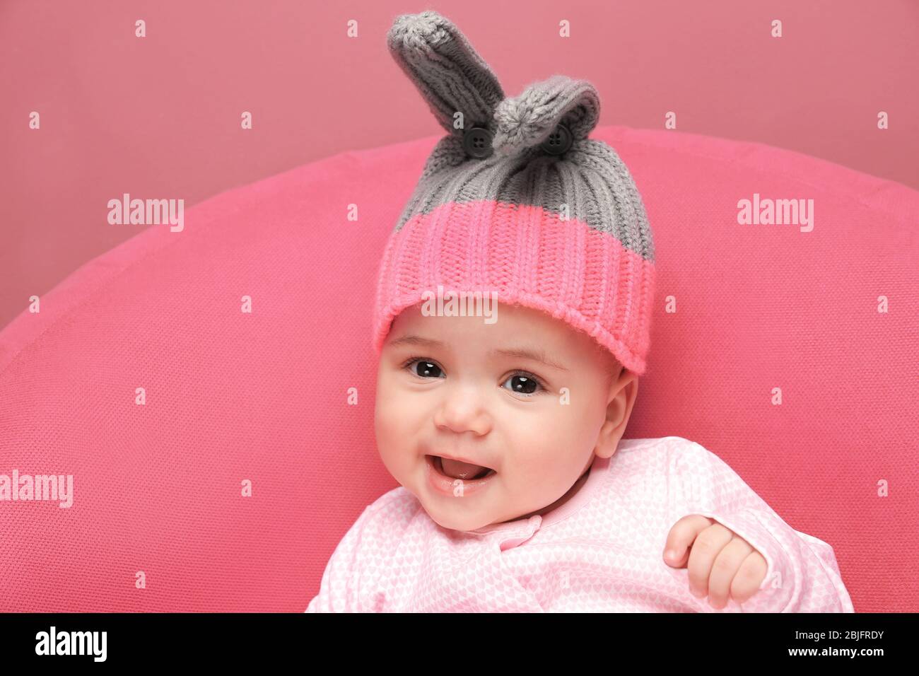 Cute little baby sitting on lounge against color background Stock Photo ...