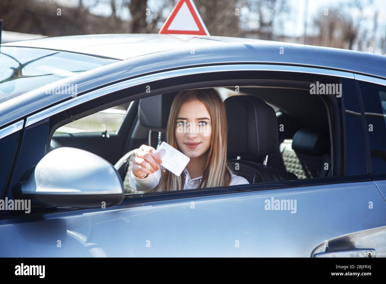 Joyful girl driving a training car with a drivers license card in her ...
