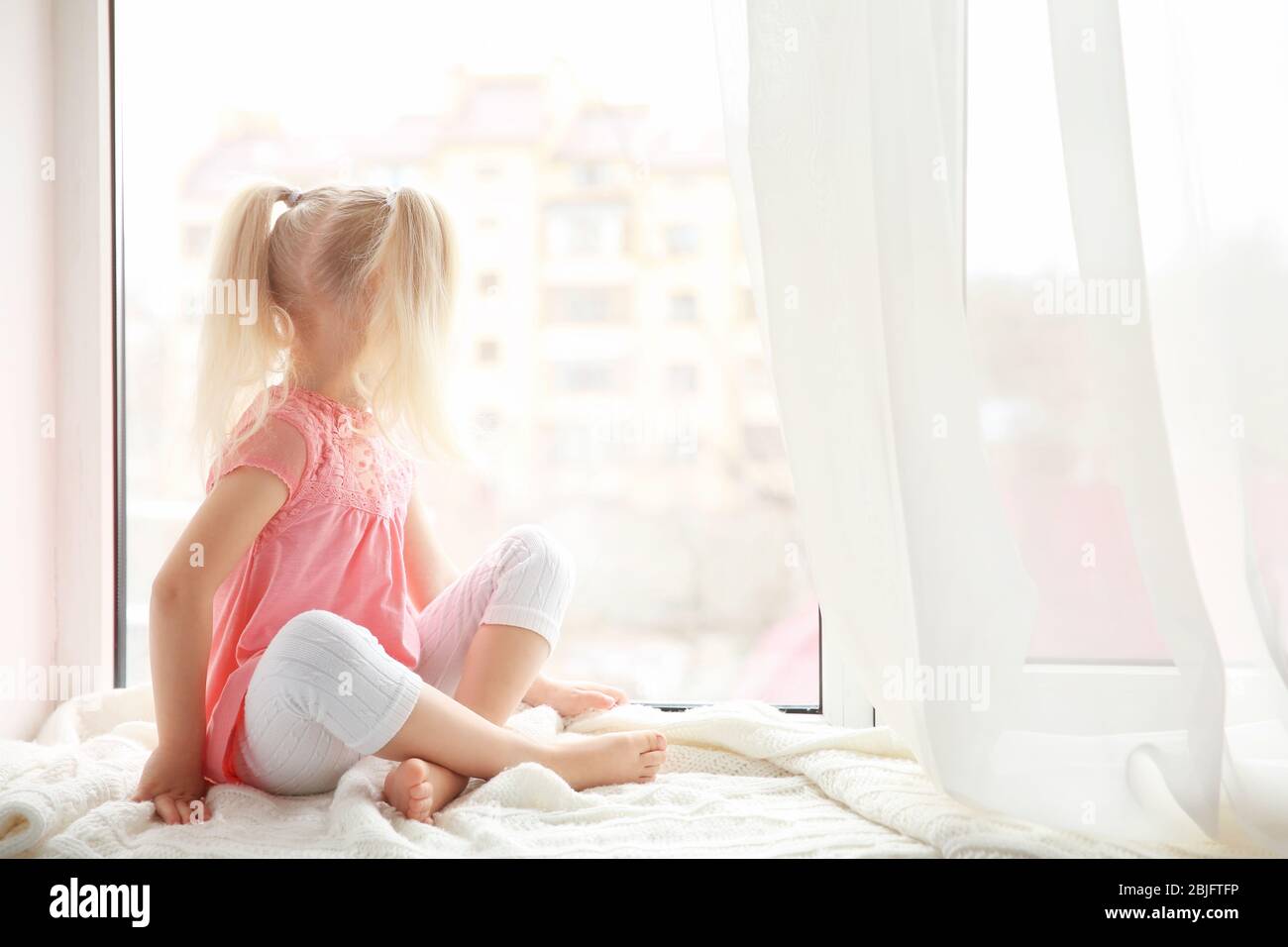 Cute little girl sitting on windowsill Stock Photo - Alamy