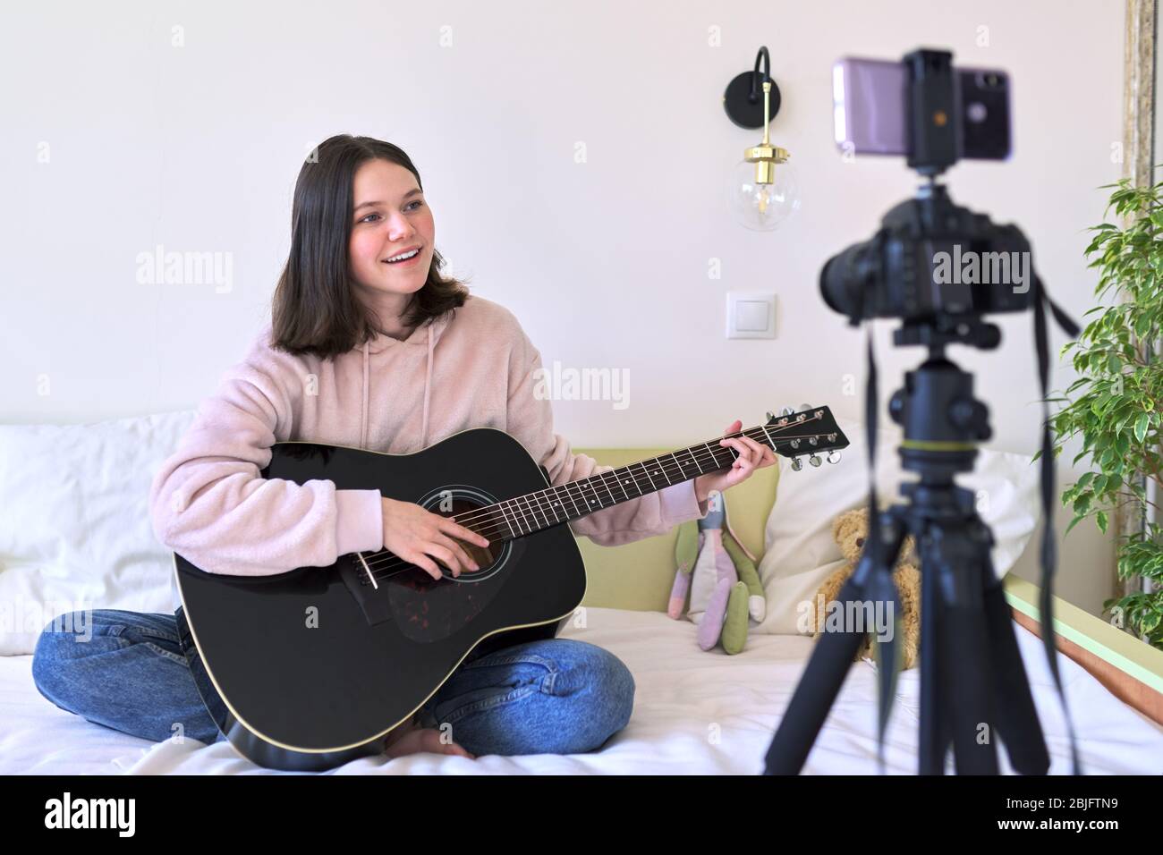 Teenage girl playing an acoustic guitar, recording video for channel ...