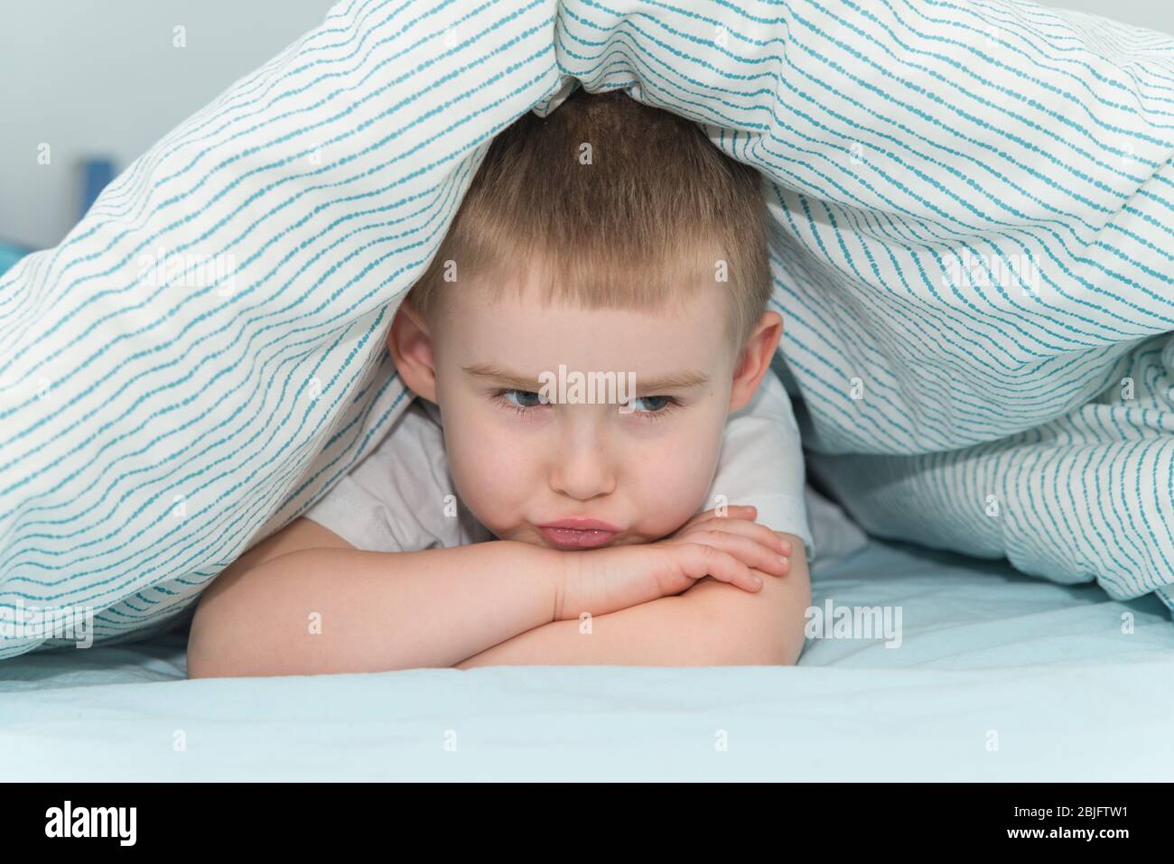 offended little boy lays under the blanket and looks right. Cute ...