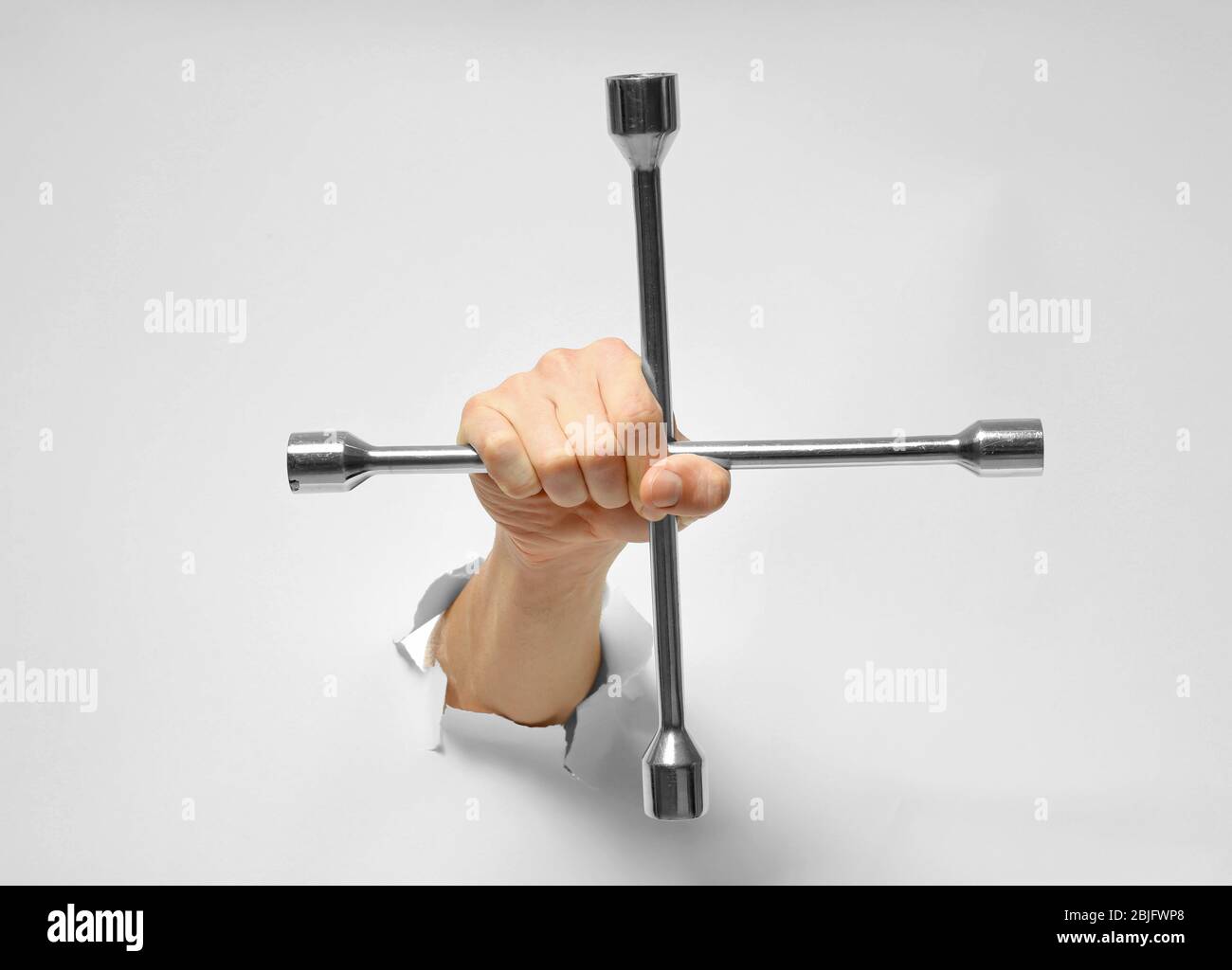 Hand of auto mechanic with wheel wrench tearing white paper background ...