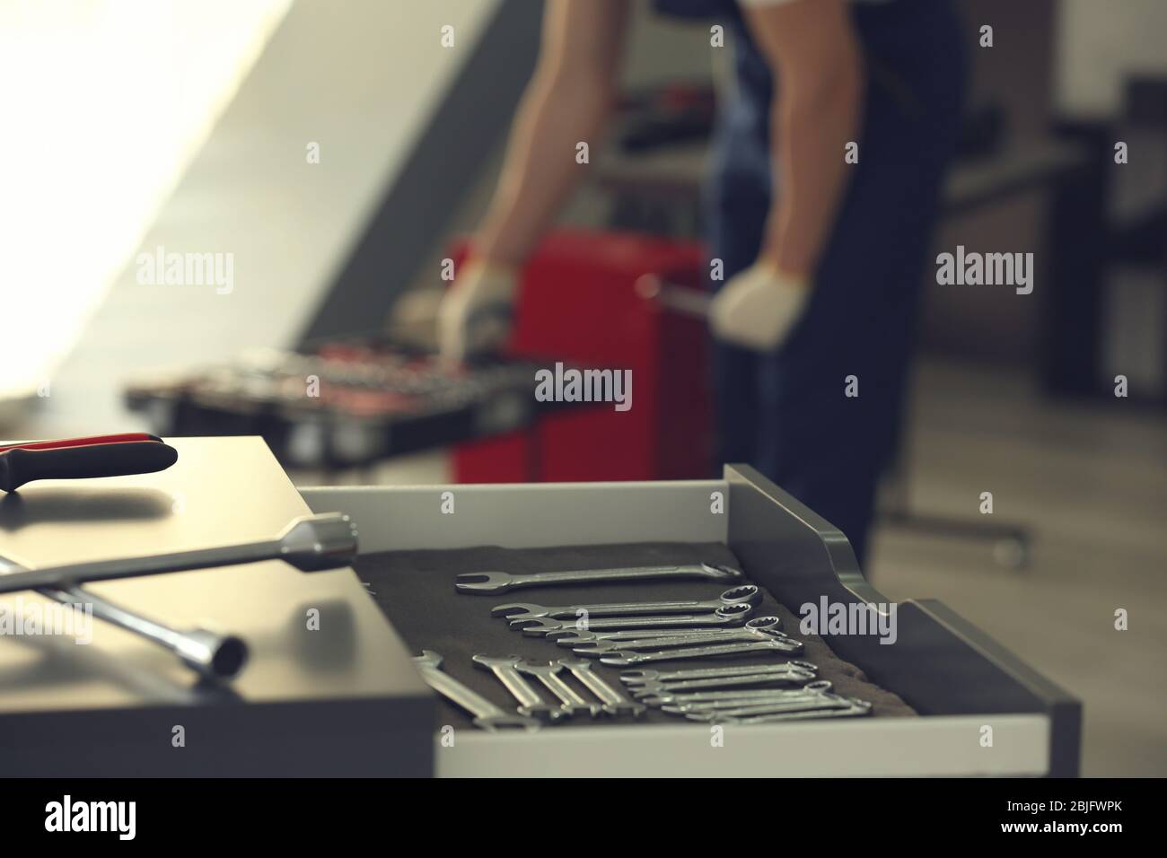 Drawer unit with tools in car repair shop and blurred auto mechanic on ...