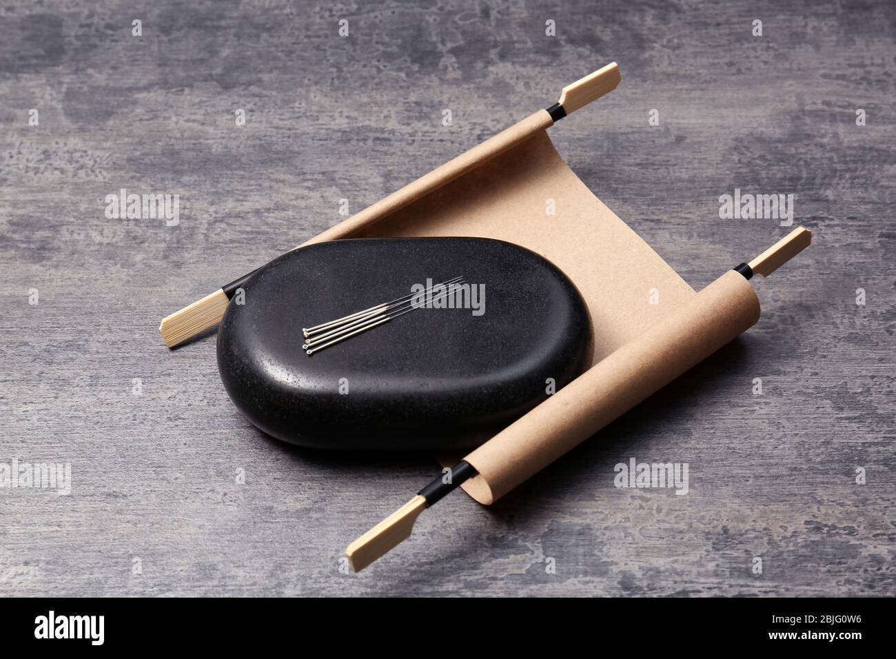 Stone with acupuncture needles and scroll on grey background Stock ...