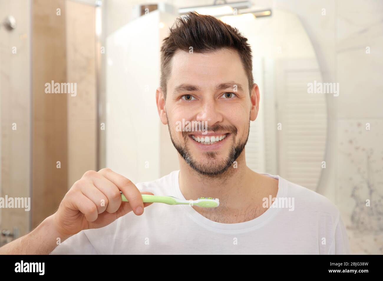 Handsome young man brushing teeth in bathroom Stock Photo - Alamy